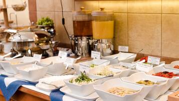 Buffet com diversas opções de comida, incluindo massas, saladas e outros pratos, dispostos sobre uma mesa com um americano azul.