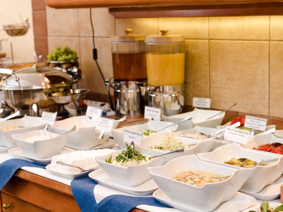 Buffet com diversas opções de comida, incluindo massas, saladas e outros pratos, dispostos sobre uma mesa com um americano azul.