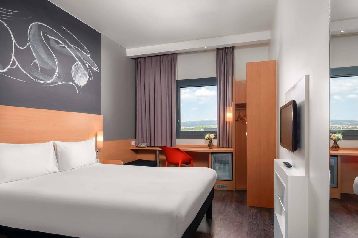 Quarto de hotel com cama, escrivaninha, cadeira, televisão e vista para a cidade.