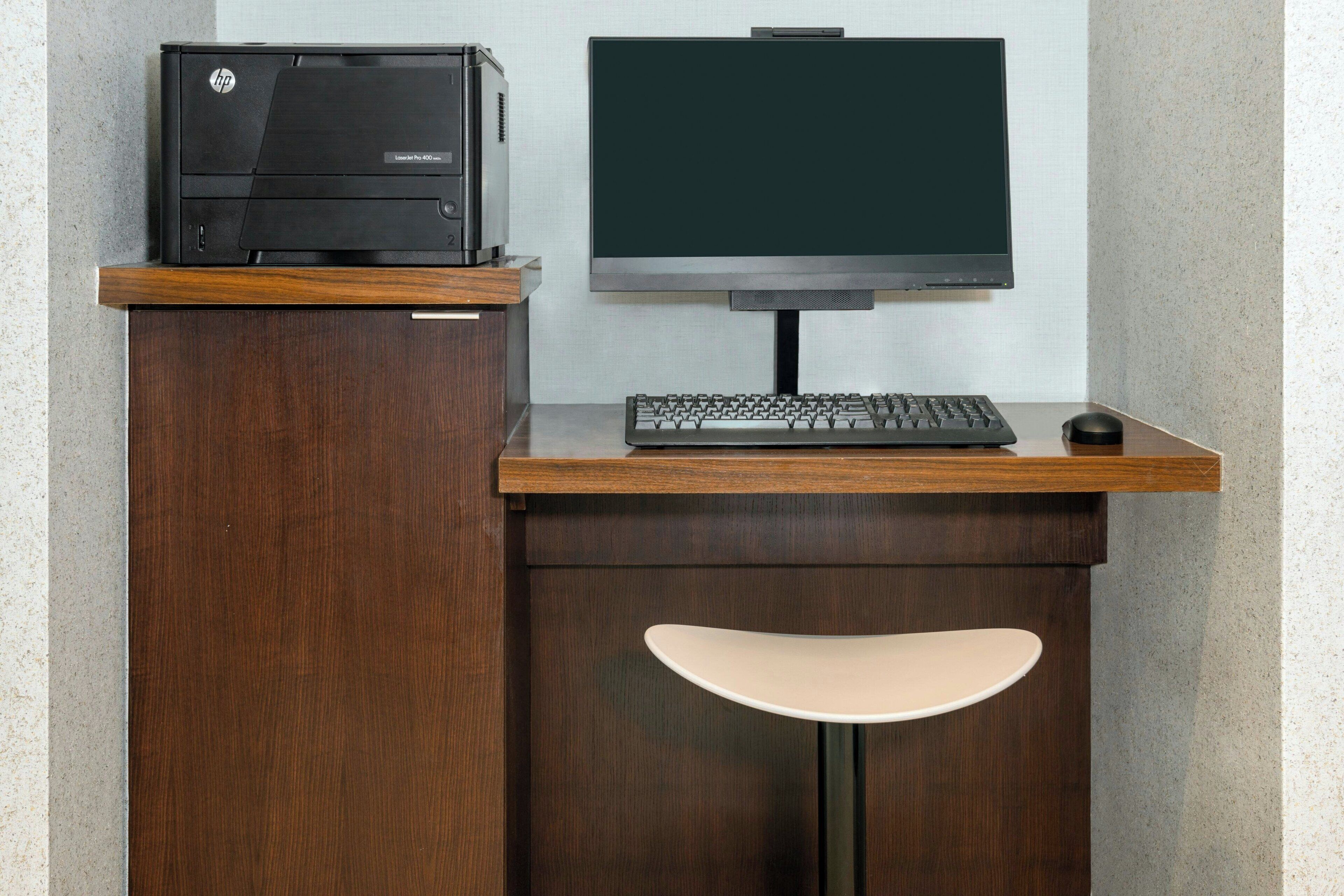 Um espaço de escritório compacto com uma impressora HP, um monitor, um teclado e uma cadeira.