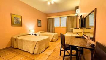 Quarto de hotel com duas camas, uma escrivaninha, uma cadeira, um abajur, um espelho e uma janela com cortinas.
