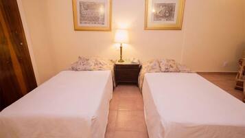 Quarto com duas camas de solteiro, mesa de cabeceira com abajur e duas imagens emolduradas na parede.