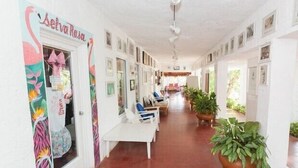 Um corredor com paredes brancas, quadros e plantas em vasos.