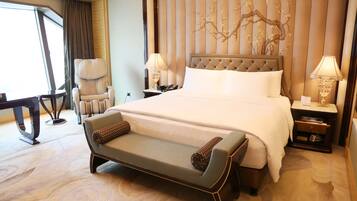 Quarto de hotel com uma cama grande, um banco, uma escrivaninha e uma cadeira.