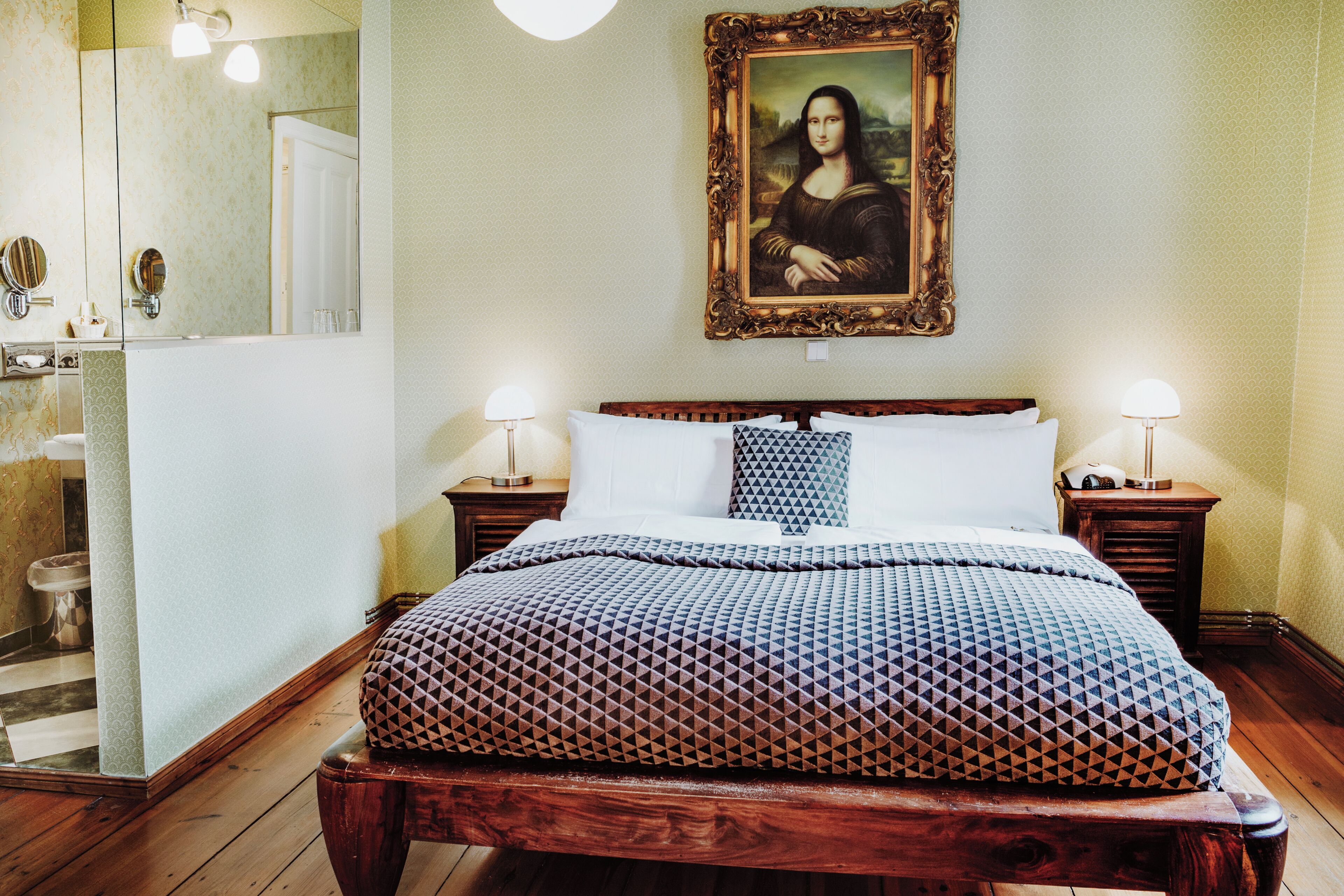 Quarto com cama, duas mesas de cabeceira, um criado-mudo, um espelho e uma obra de arte emoldurada na parede.