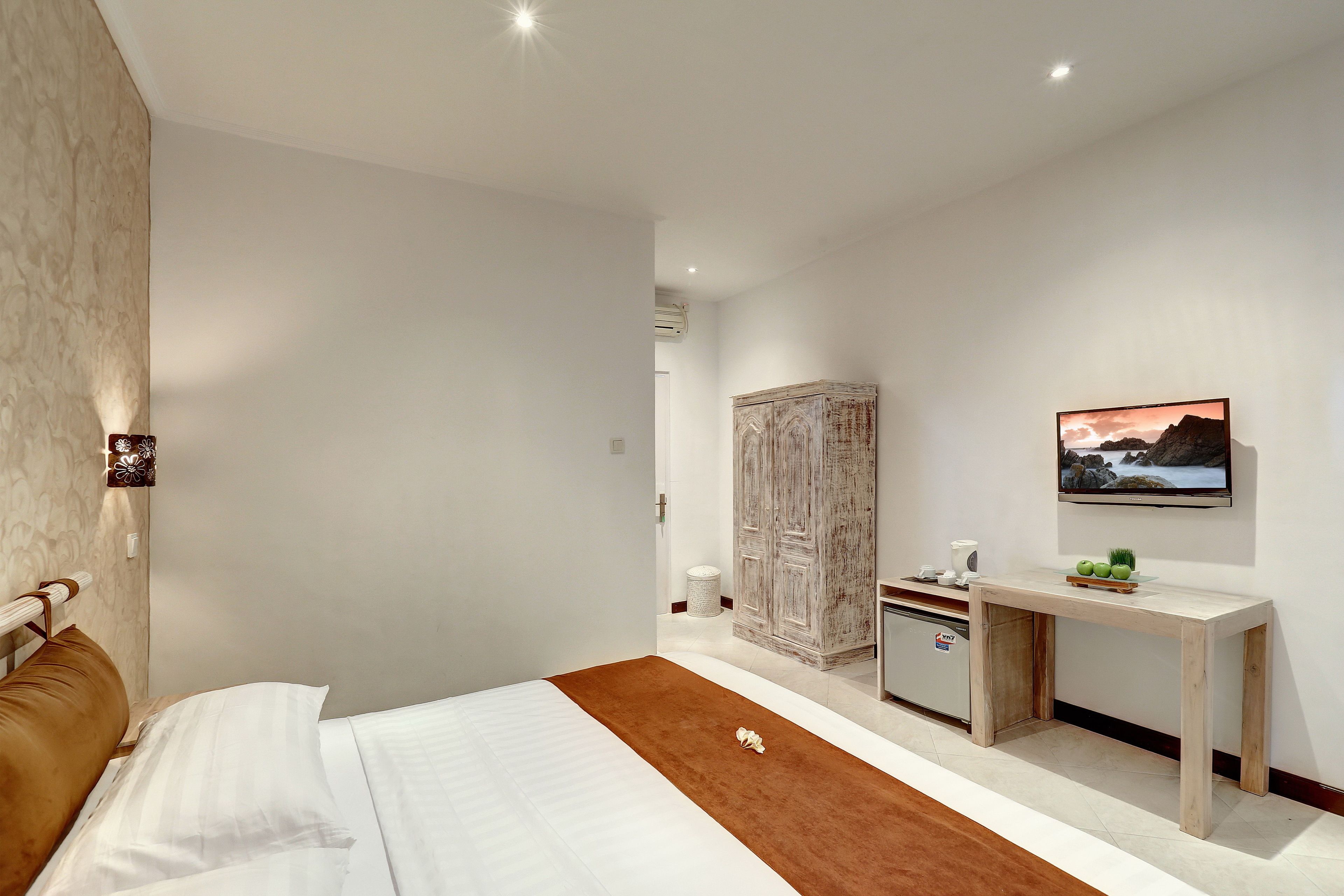 Quarto de hotel moderno com uma cama, uma secretária de madeira, uma televisão e um guarda-roupa.