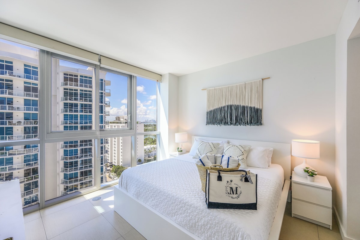 Quarto de hotel moderno com uma janela grande, uma cama bem arrumada e vista para a cidade.