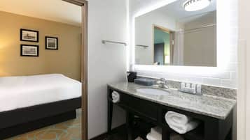 Quarto de hotel com cama, banheiro com pia e espelho, e um porta-toalhas.