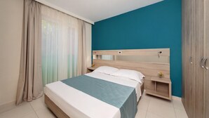 Quarto de hotel com cama, mesa de cabeceira, cabeceira de madeira, parede de destaque azul-turquesa e guarda-roupa.