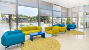 Um lobby moderno com grandes janelas, sofás amarelos e azuis, e uma mesa de centro azul.