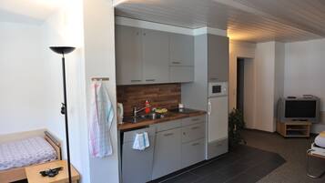 Cozinha compacta com micro-ondas, pia e bancada de madeira. Há uma pequena TV e uma mesa de cabeceira com abajur.