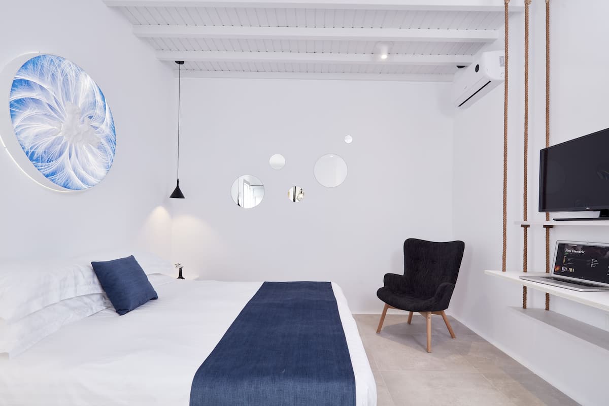 Quarto de hotel moderno com uma cama grande, uma poltrona preta, uma televisão e um ar condicionado fixado na parede.