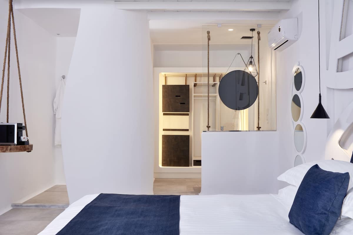 Quarto moderno com uma cama grande, luminária pendente e parede branca com espelhos redondos.