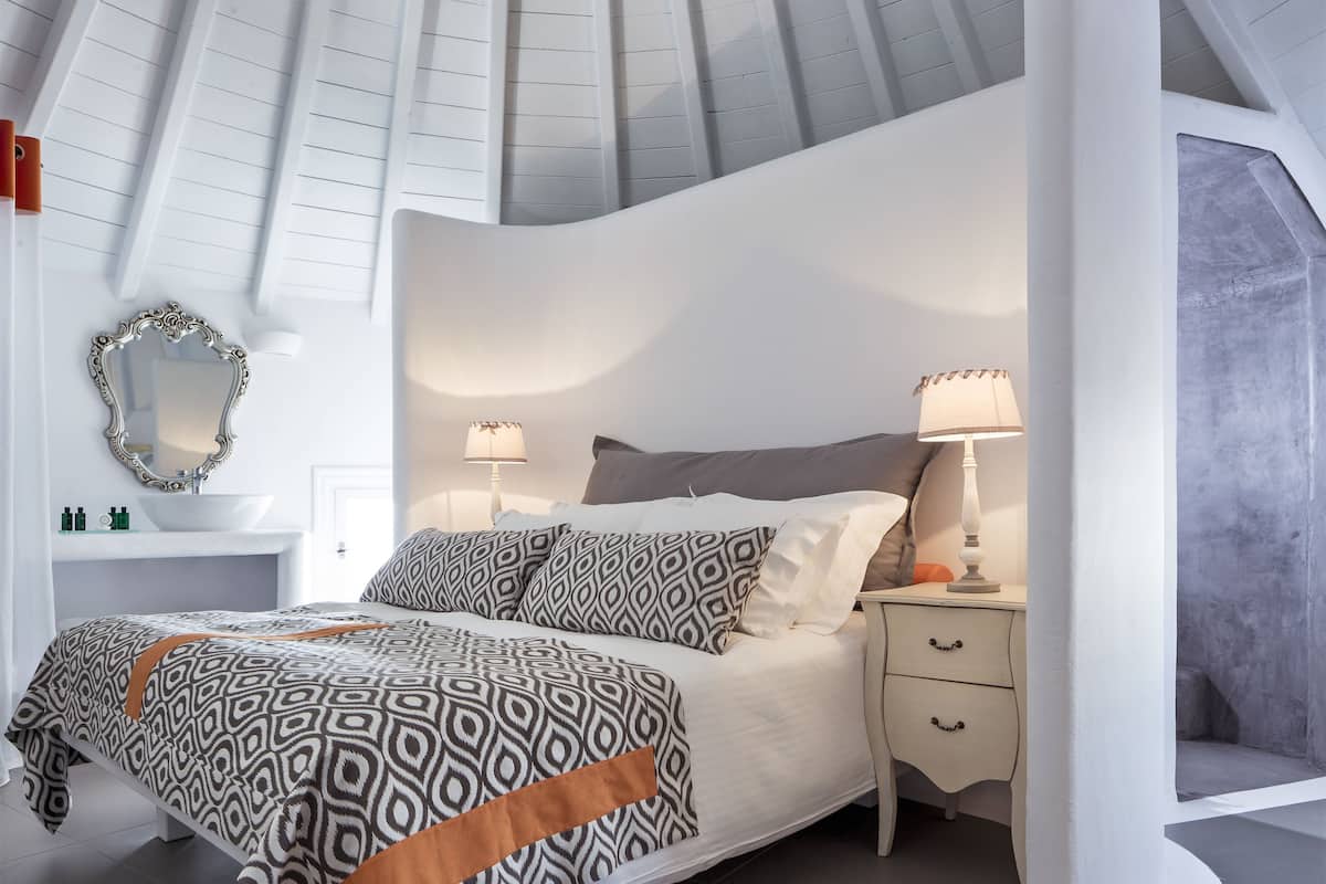 Um quarto com teto inclinado, uma cama com roupa de cama estampada, luminárias de cabeceira, um espelho e uma pequena mesa de cabeceira.