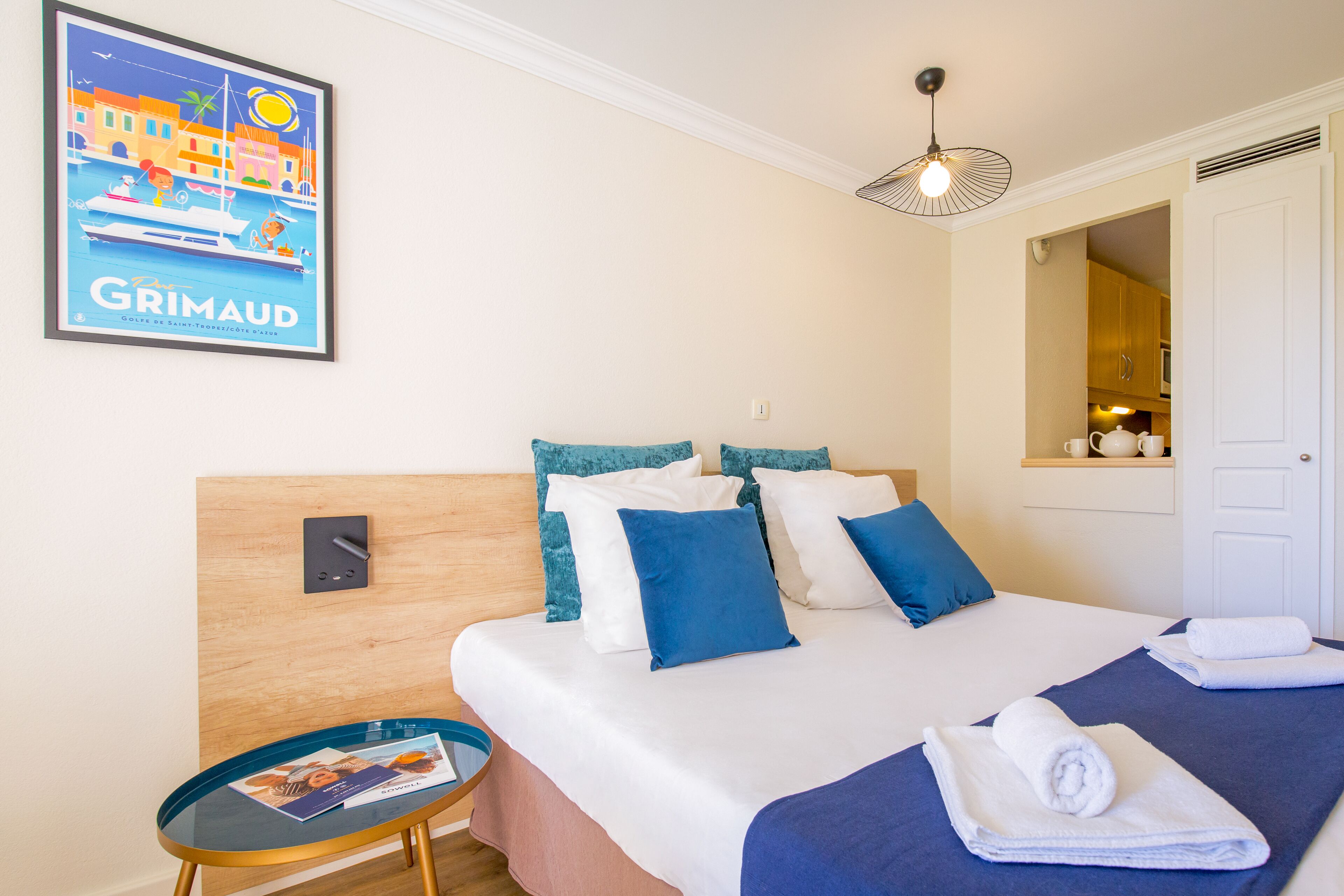 Quarto de hotel com cama, uma mesa pequena e um cartaz na parede.