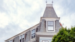 Uma casa grande de dois andares, com um telhado pontiagudo destacado e uma chaminé decorativa.