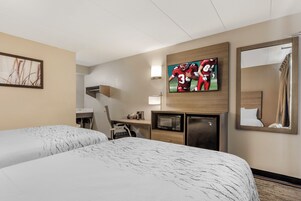 Quarto de hotel com duas camas, televisão de tela plana na parede, escrivaninha com cadeira, micro-ondas e geladeira.