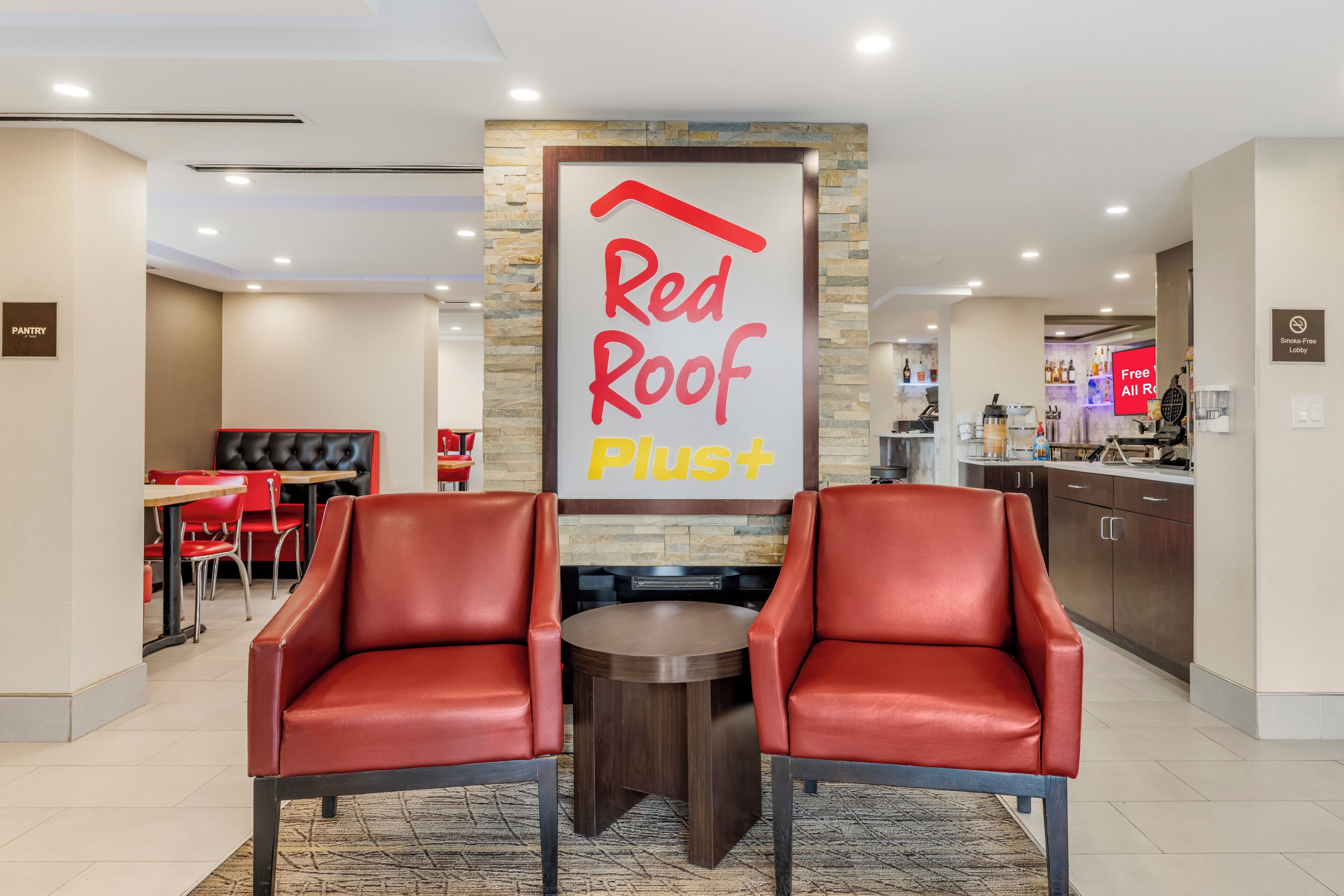 Área de convívio Red Roof Plus com poltronas de couro, uma mesa pequena e uma parede de detalhes em pedra.