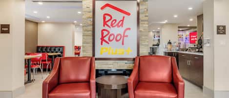 Área de convívio Red Roof Plus com poltronas de couro, uma mesa pequena e uma parede de detalhes em pedra.