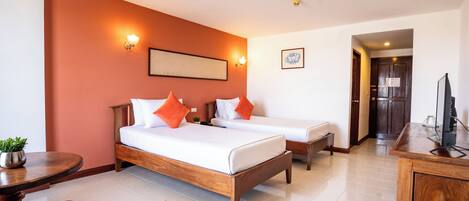 Quarto de hotel com duas camas, uma escrivaninha de madeira, uma televisão e uma pequena mesa com uma planta.