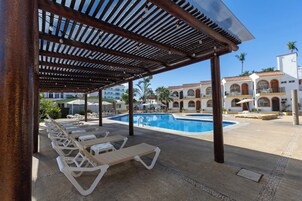 Área da piscina com espreguiçadeiras e uma pérgola coberta.