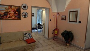 Uma sala de estar com um sofá, um quadro, um extintor de incêndio e um vaso de planta.