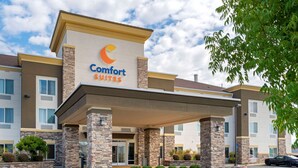 Um hotel Comfort Suites com entrada coberta, pilares de pedra e estacionamento.