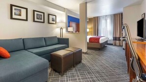 Quarto de hotel com sofá, apoio para os pés, cama, televisão e escrivaninha.
