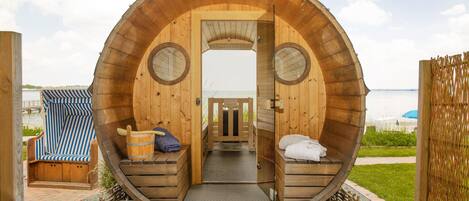 Um quarto em formato de barril de madeira com duas camas, um banco e uma pequena mesa.