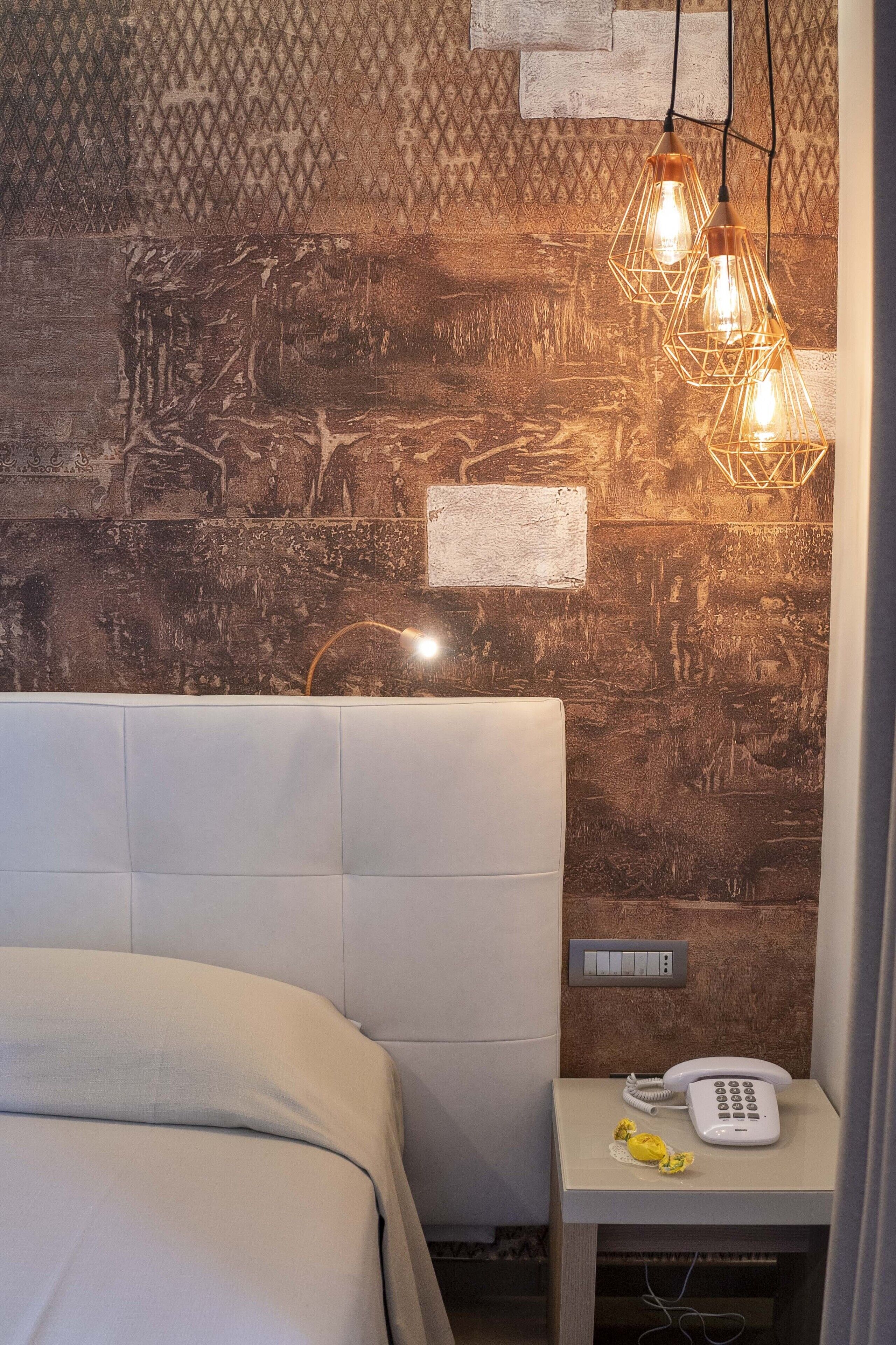 Quarto de hotel com uma cama, uma mesa de cabeceira com telefone e uma parede com um mural texturizado.