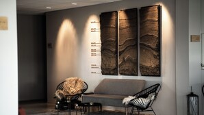 Um lobby moderno com um sofá cinzento, cadeiras pretas e uma obra de arte com textura na parede.