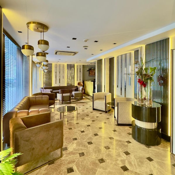 Um hall moderno com sofá, poltronas, mesa de centro e um vaso decorativo com flores.