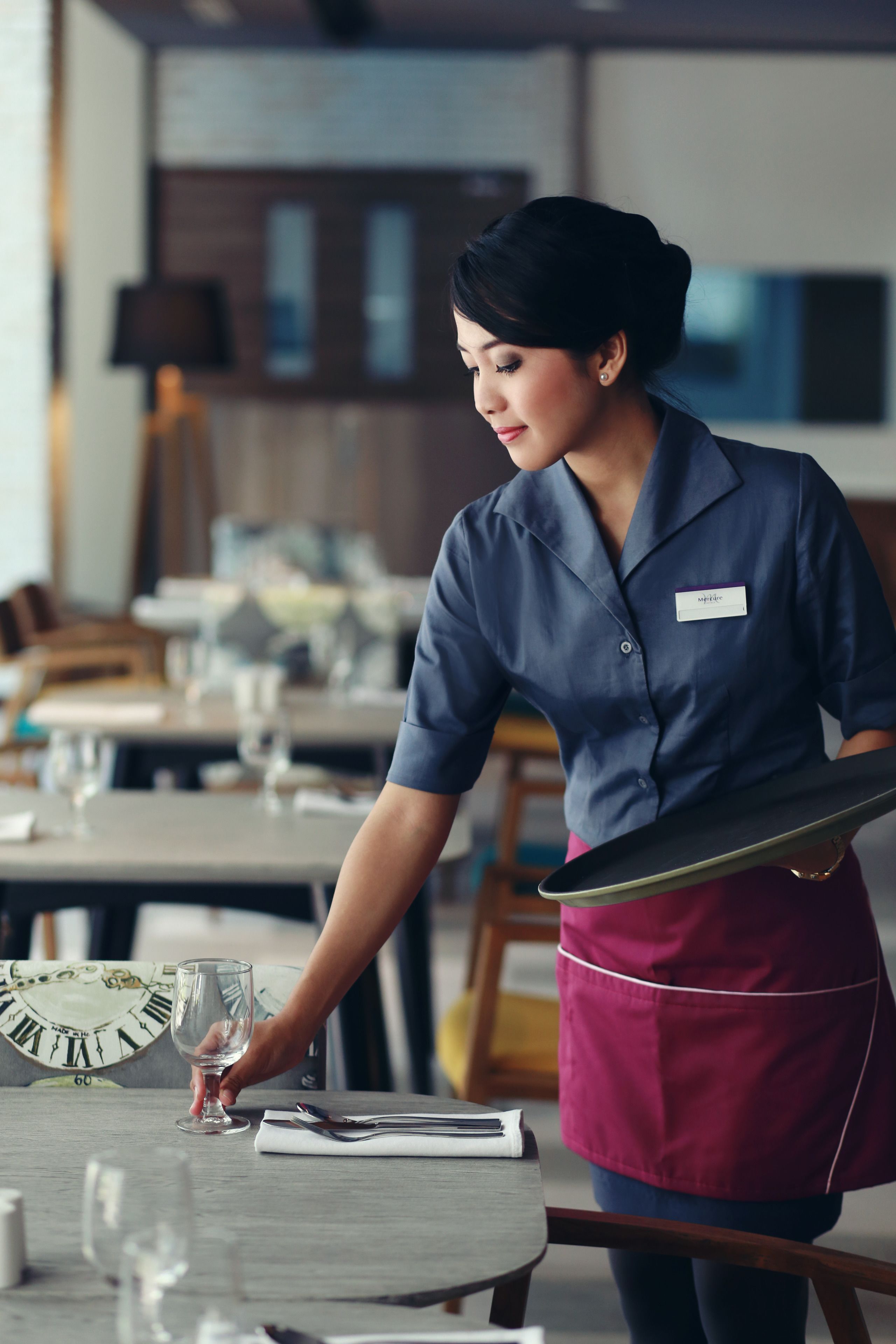 Uma pessoa vestindo uniforme serve uma mesa com um copo e um prato.