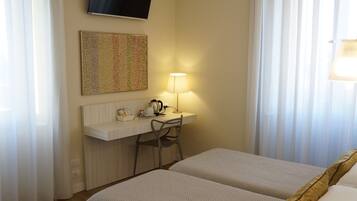 Quarto de hotel com duas camas, uma escrivaninha com cadeira, uma televisão na parede e um abajur na escrivaninha.