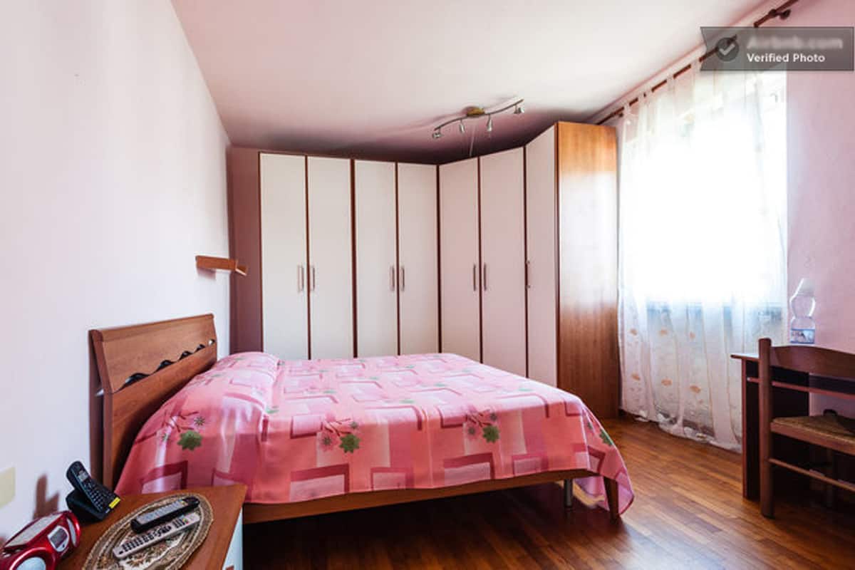 Quarto com cama, guarda-roupa de madeira e uma pequena mesa com um rádio.