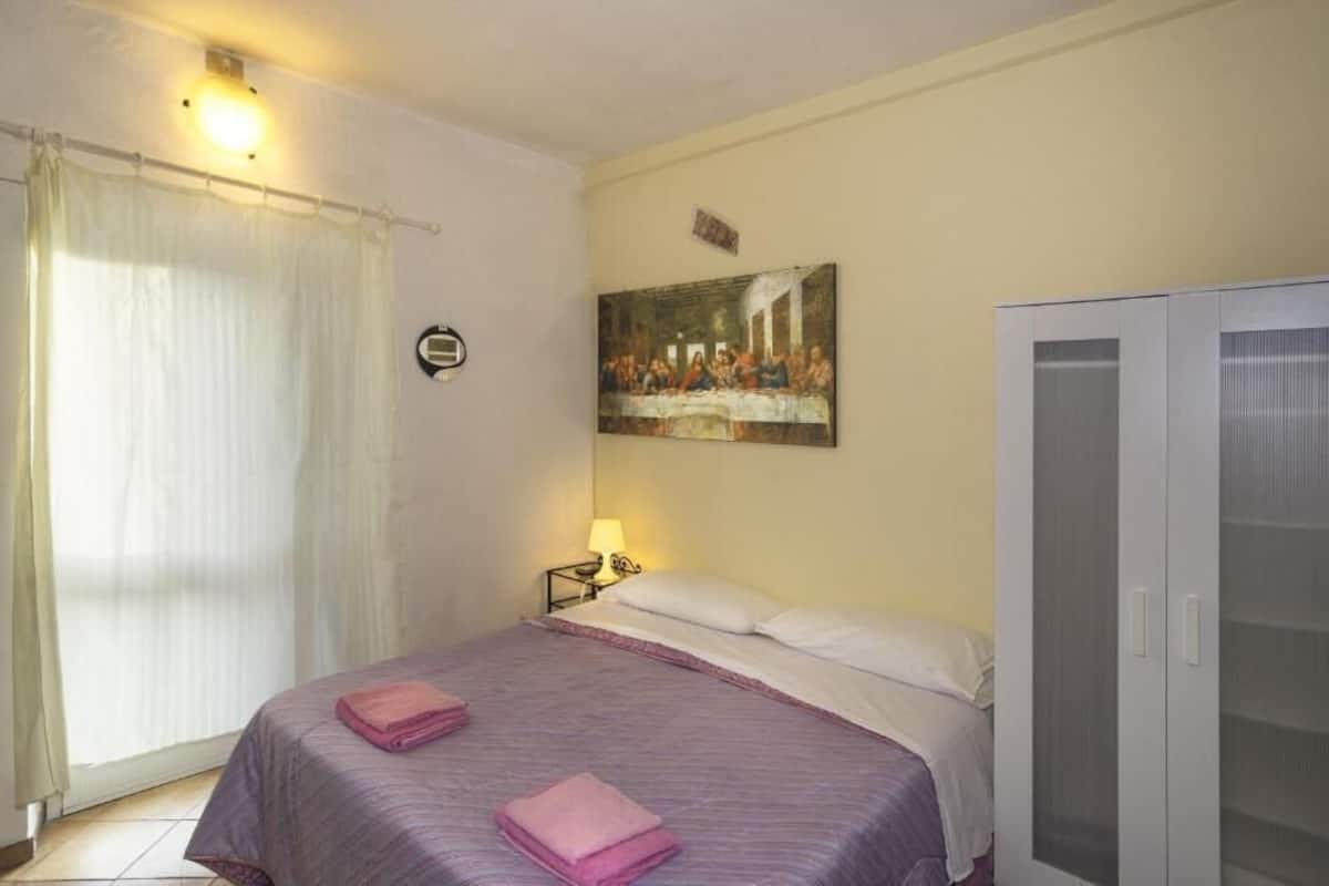 Quarto com cama, um quadro de A Última Ceia, guarda-roupa e mesa de cabeceira com abajur.