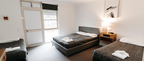 Quarto de hotel com duas camas, uma mesa, uma cadeira, uma luminária e um quadro na parede.