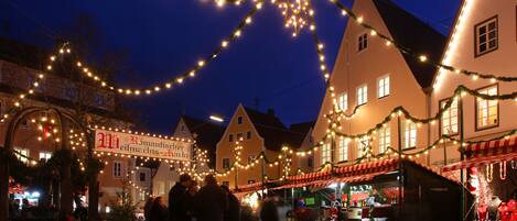 Um mercado tradicional europeu com bancas e edifícios, decorado com luzes e guirlandas.