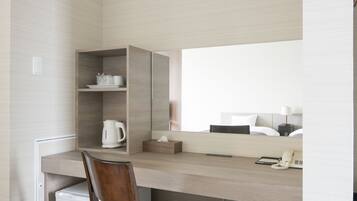 Quarto de hotel moderno com uma escrivaninha de madeira, uma cadeira, máquina de café, caixa de lenços, telefone e espelho.