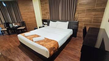 Quarto de hotel com uma cama grande, uma escrivaninha, cadeiras e piso de madeira.