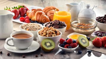 Mesa de café da manhã com croissants, frutas, cereais e bebidas.