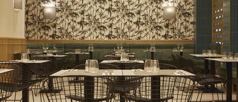 Um restaurante com mesas e cadeiras, parede estampada e área com assentos em cabine verde.