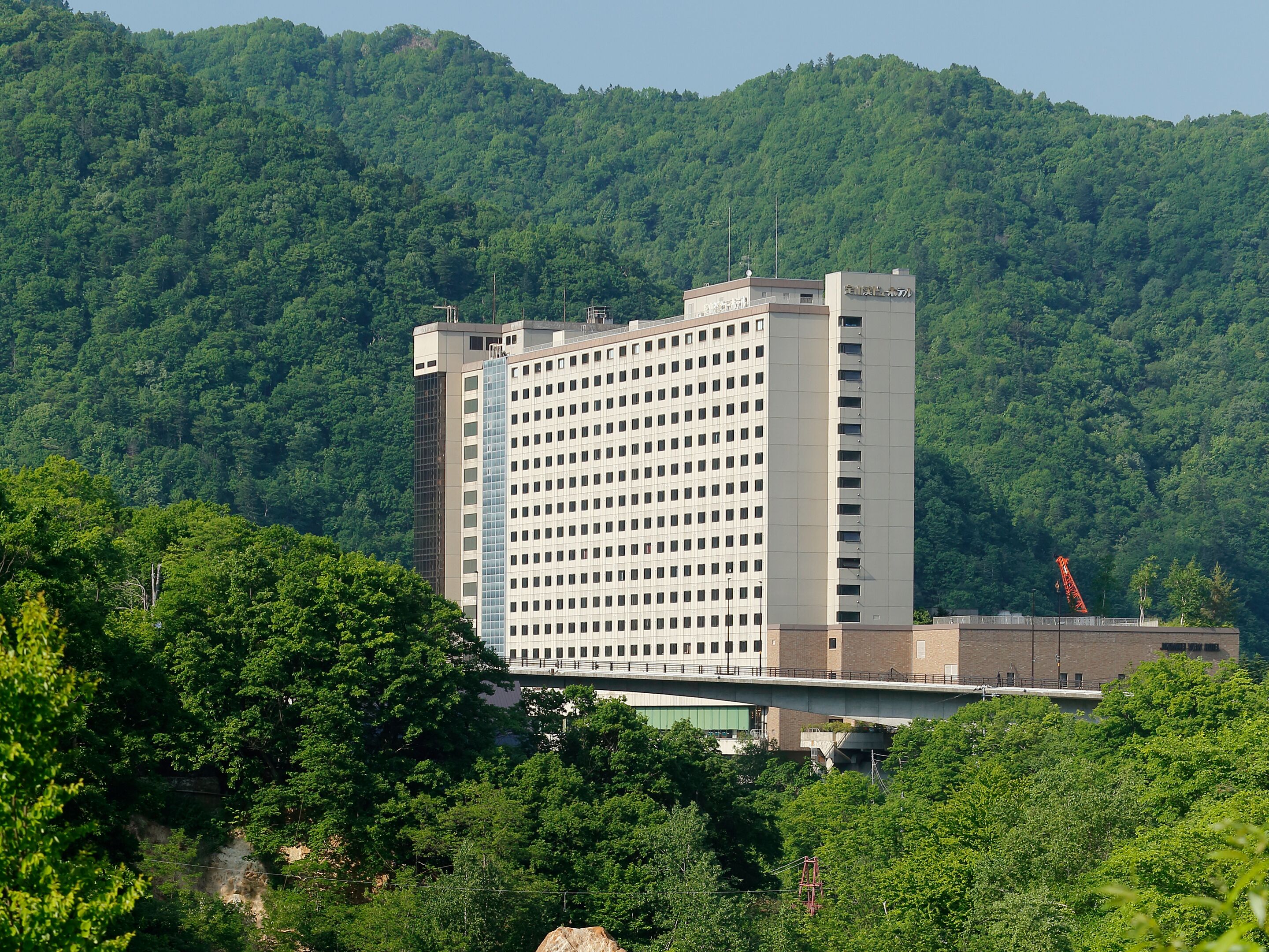 Um edifício de hotel alto com design moderno, rodeado por colinas verdejantes.