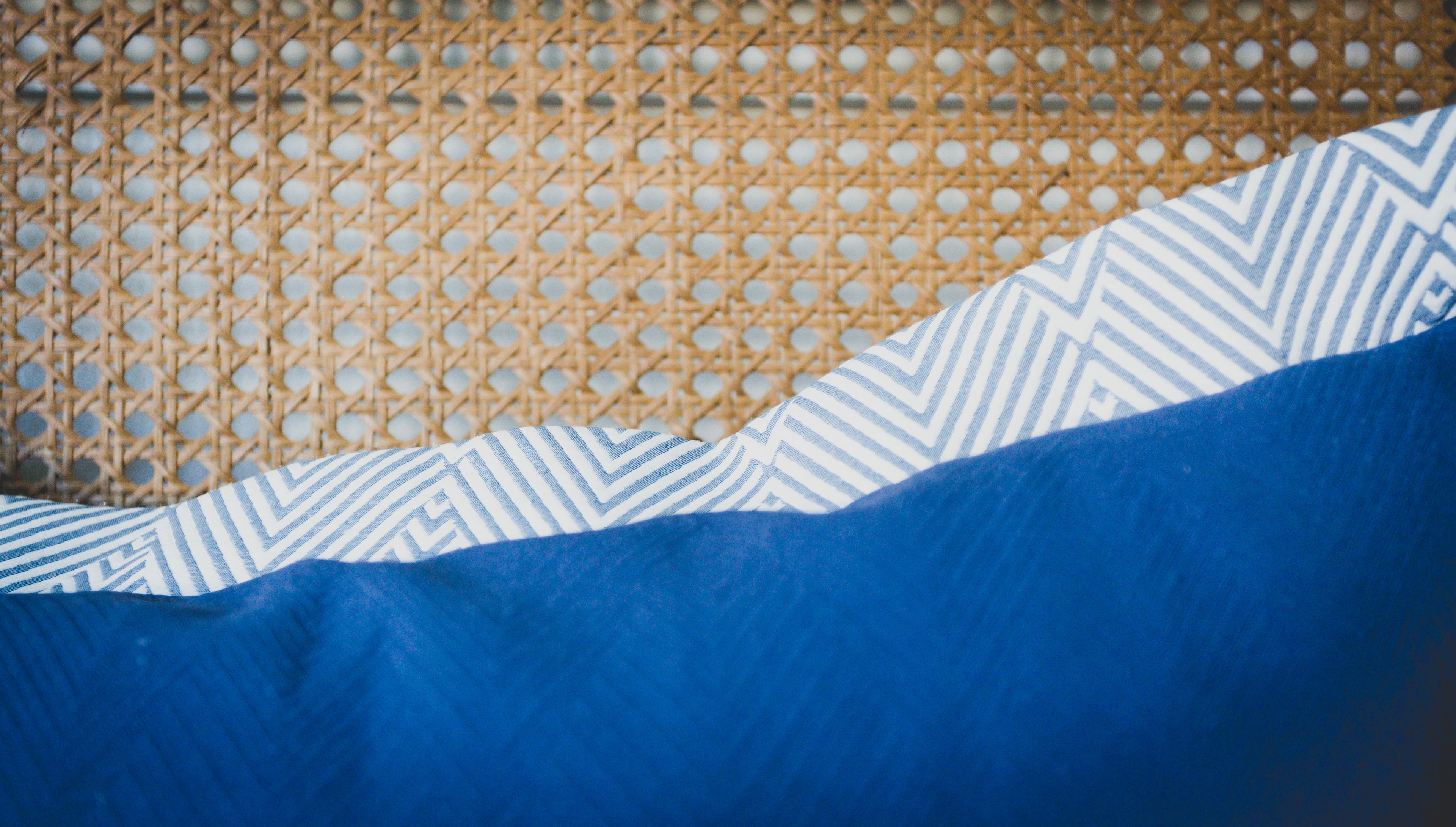 Cama com travesseiro azul e branco listrado e cabeceira trançada.