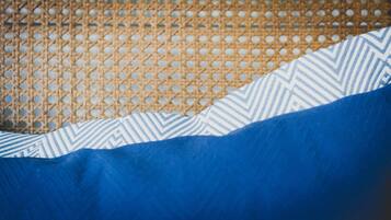 Cama com travesseiro azul e branco listrado e cabeceira trançada.