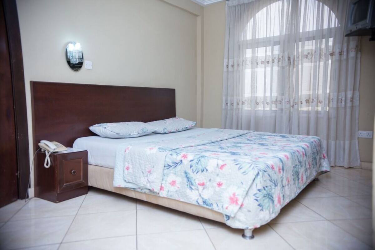 Quarto com cama, mesa de cabeceira, telefone e janela com cortinas.