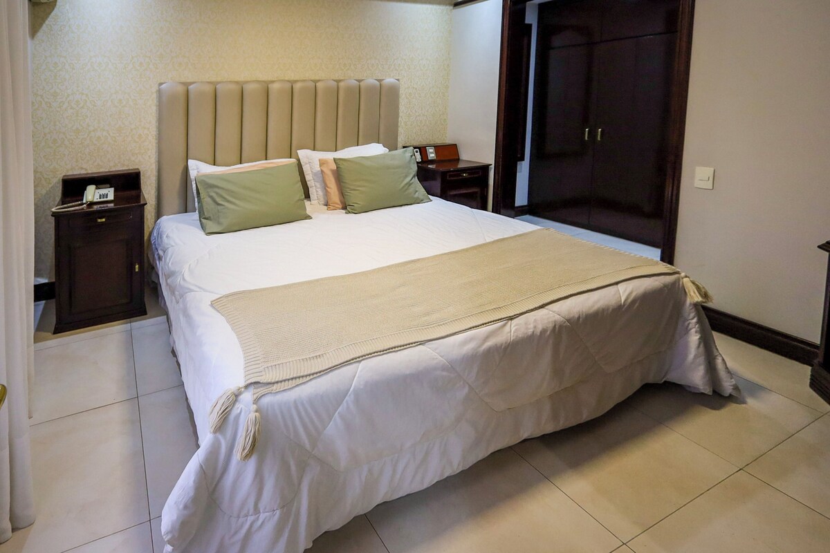 Quarto de hotel com uma cama grande, mesa de cabeceira com telefone e um guarda-roupa.