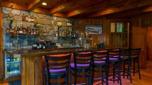 Uma área de bar com parede de pedra, balcão de madeira e várias garrafas de bebidas.