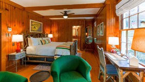 Quarto com decoração em madeira, com uma cama, duas mesas de cabeceira, escrivaninha, cadeira e janela com cortinas.