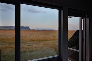 Quarto com uma janela ampla que oferece vista para uma paisagem plana e montanhas ao longe.